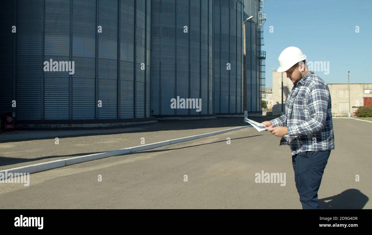 Professional engineer with blueprints inspecting agricultural silos ...