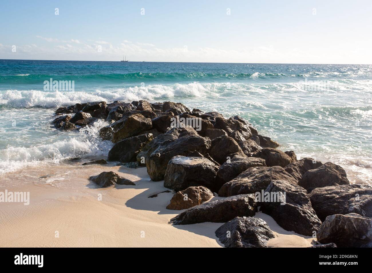 Blue sea waves crash on outcrop of black rocks on sandy Barbados beach ...