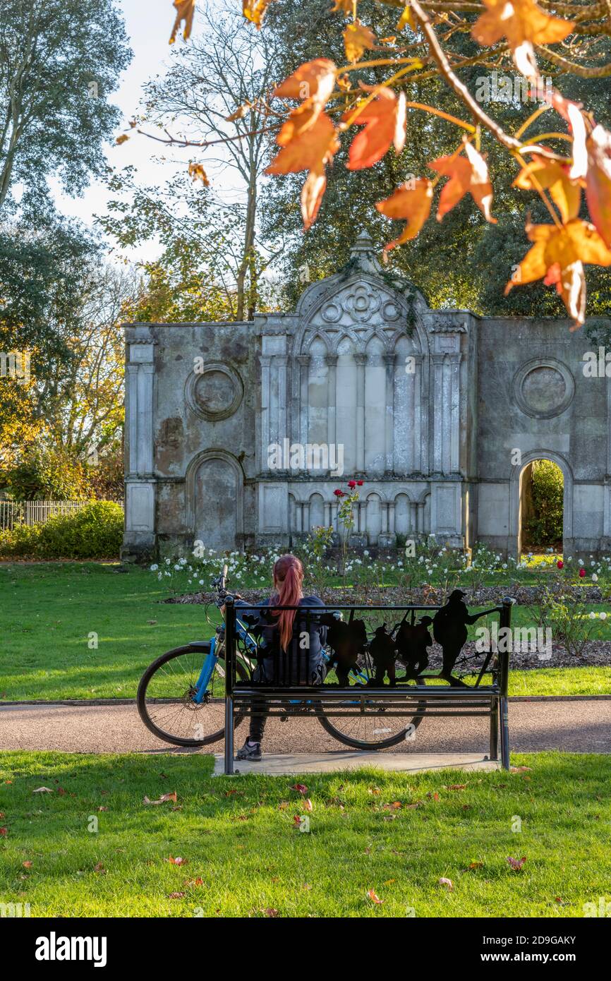 young woman sitting on a park bench in the autumn with her bicycle ...