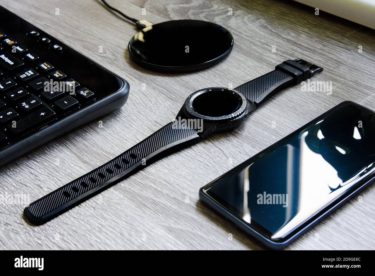 Smartphone and smartwatch next to a wireless charger and keyboard on a ...