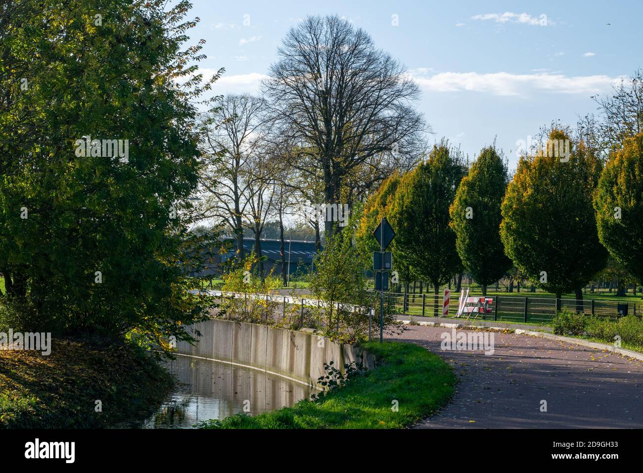 Cycle path in a bend between a row of trees and a ditch with reflection ...