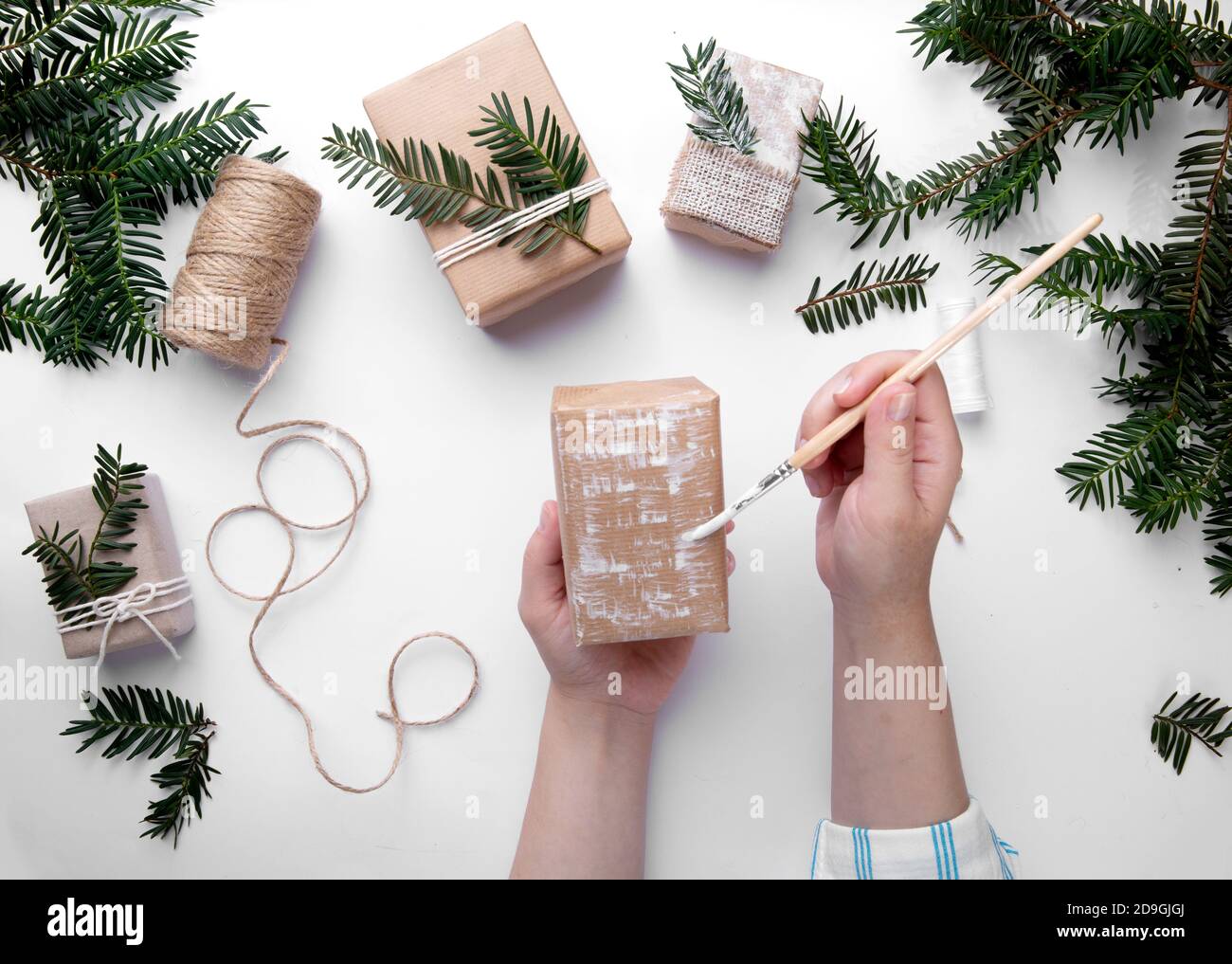 Hands hold one Christmas present and decorate it with white paint on ...