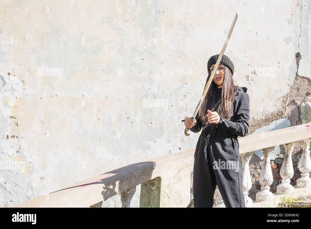 A young girl in black clothes holds a sword in front of her and is ...