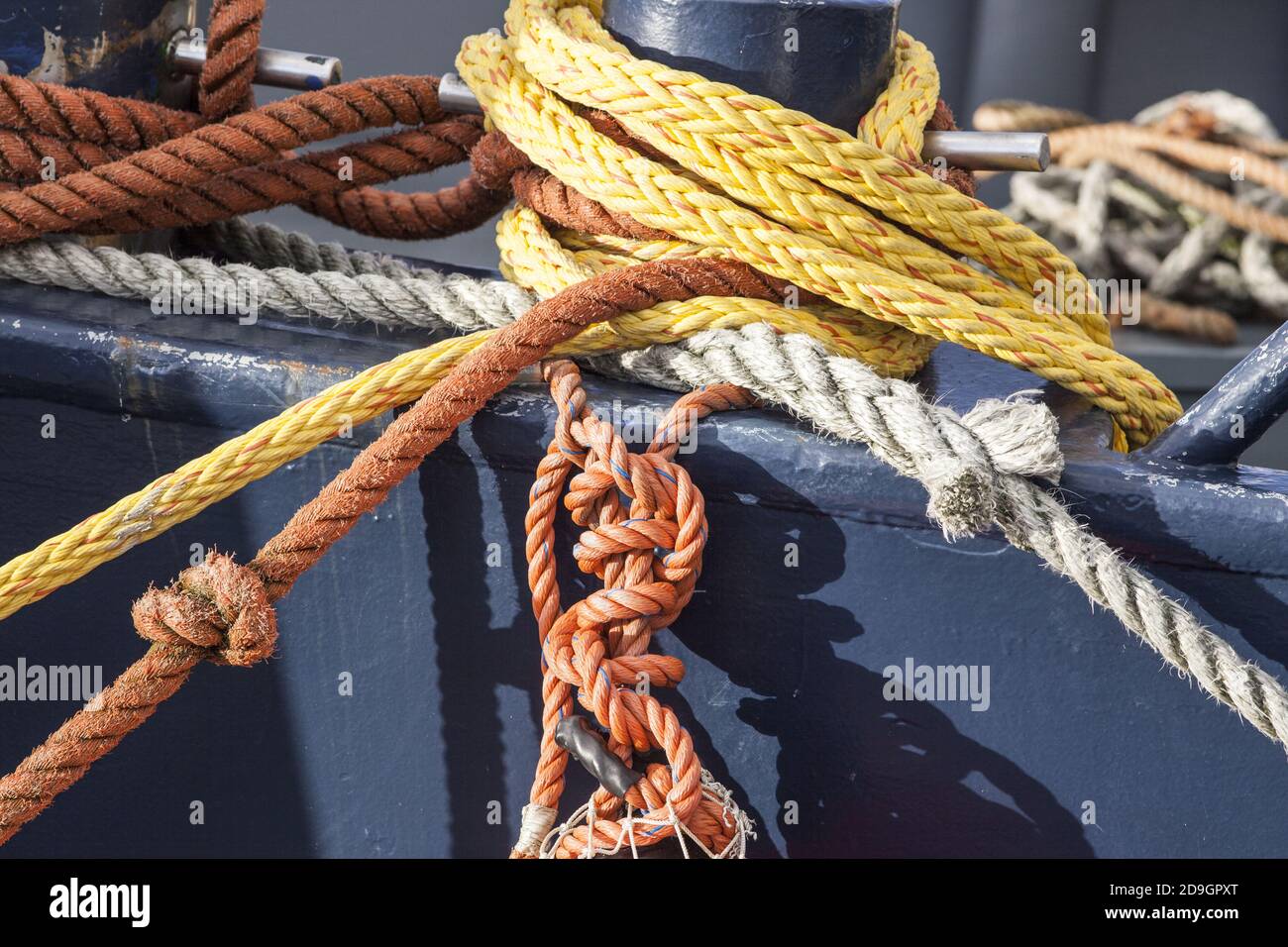 Closeup of different colored ropes tied on a grey thick pole on a boat ...