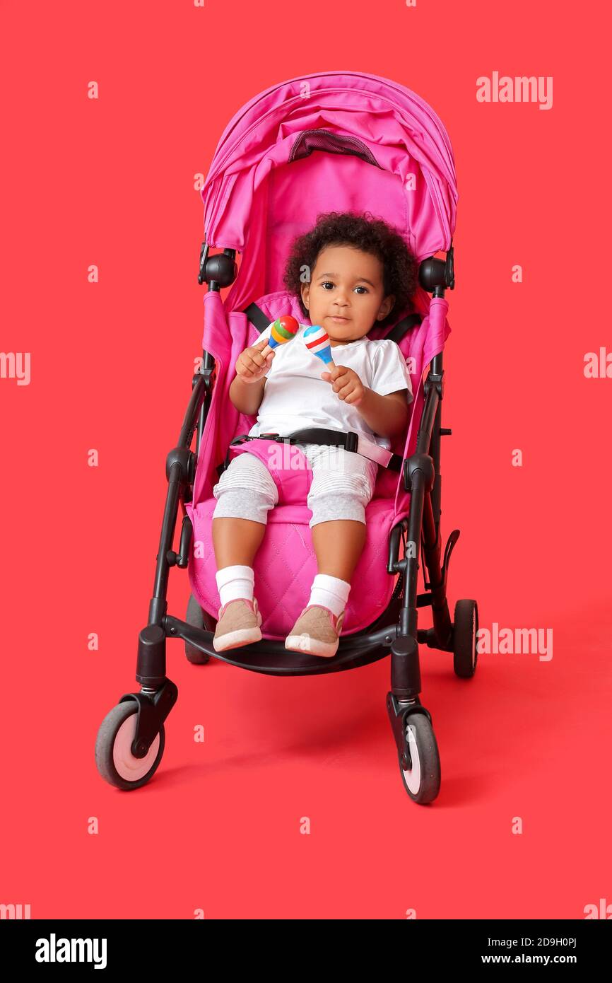 Cute African-American baby in stroller on color background Stock Photo ...