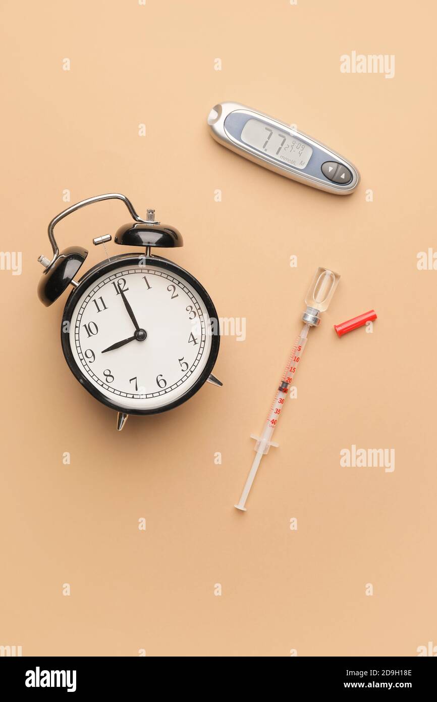 Glucometer with alarm clock, syringe and bottle of insulin on color ...