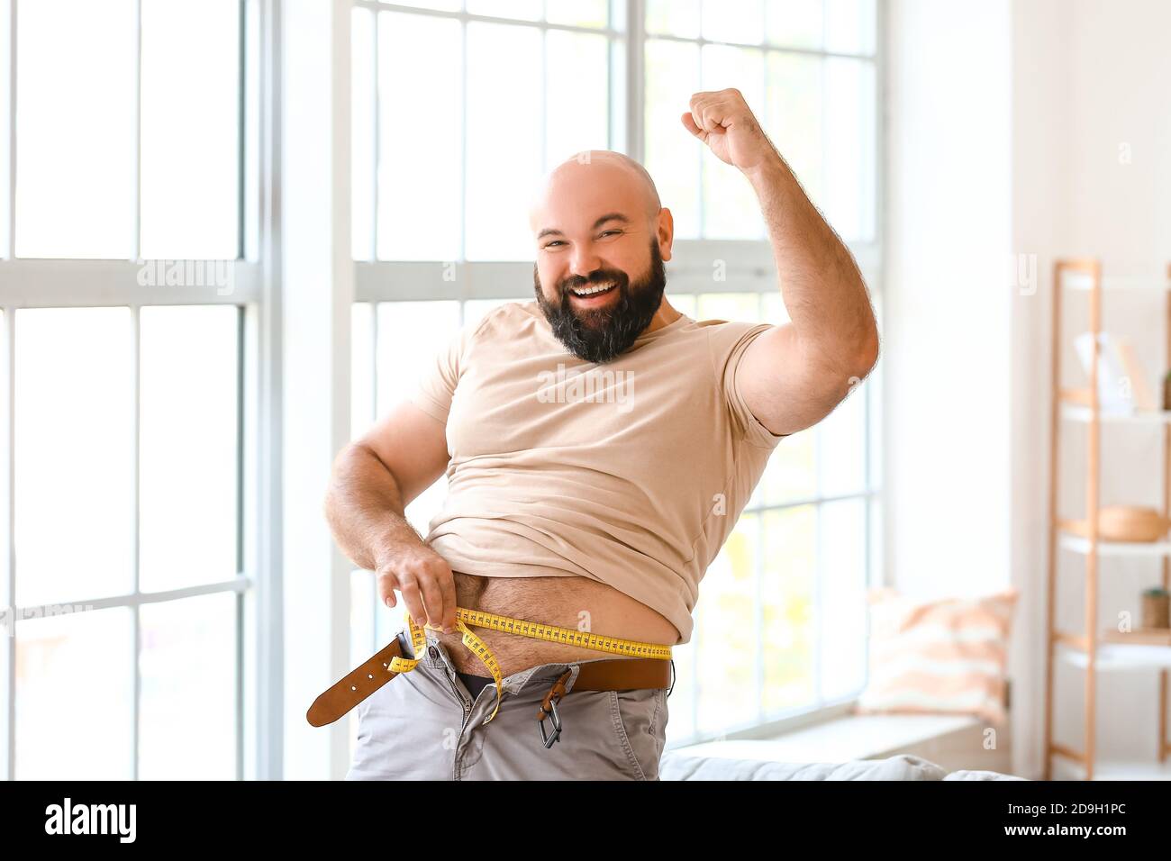 Happy overweight man measuring his waist at home. Weight loss concept ...