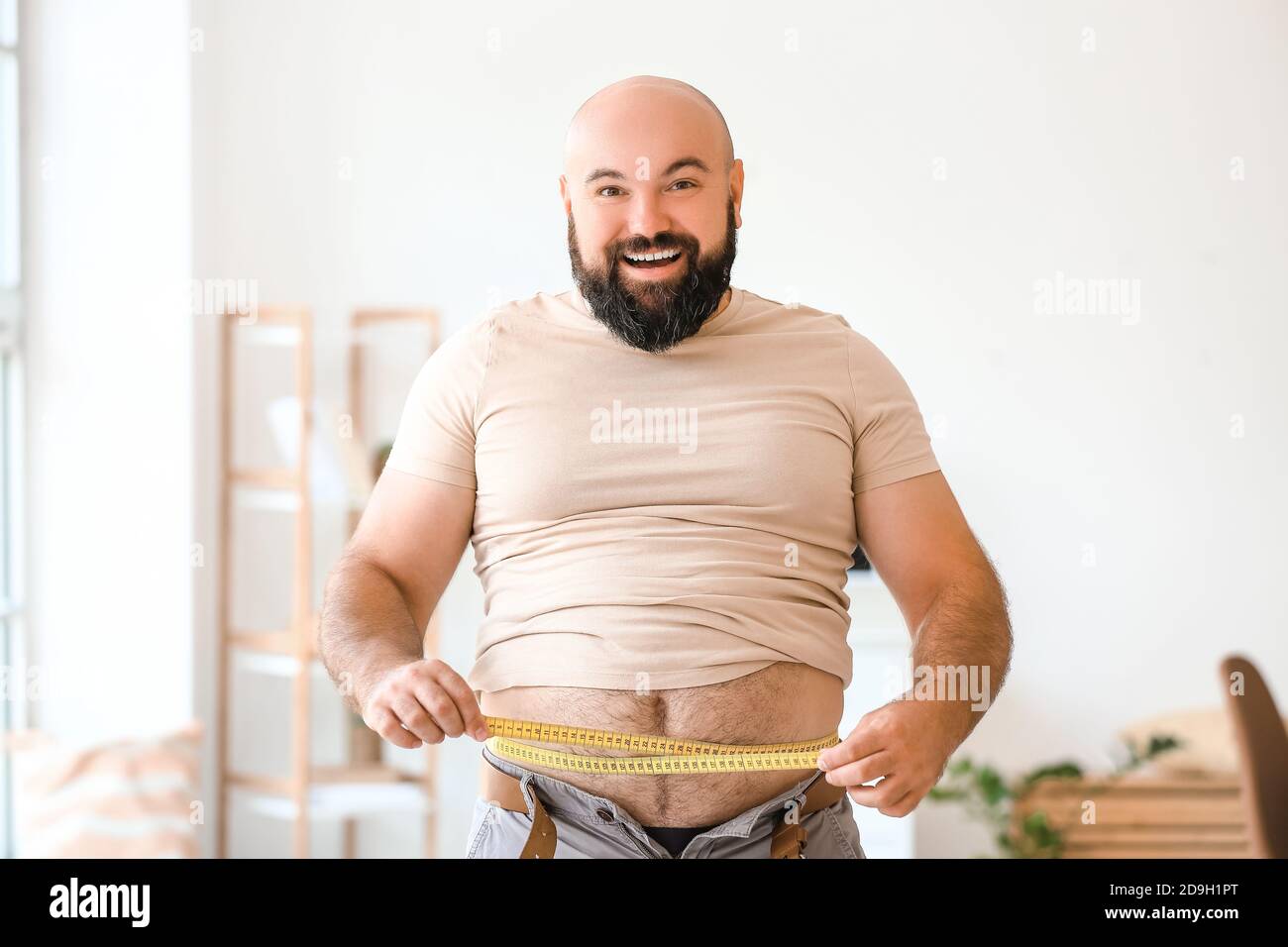 Happy overweight man measuring his waist at home. Weight loss concept ...