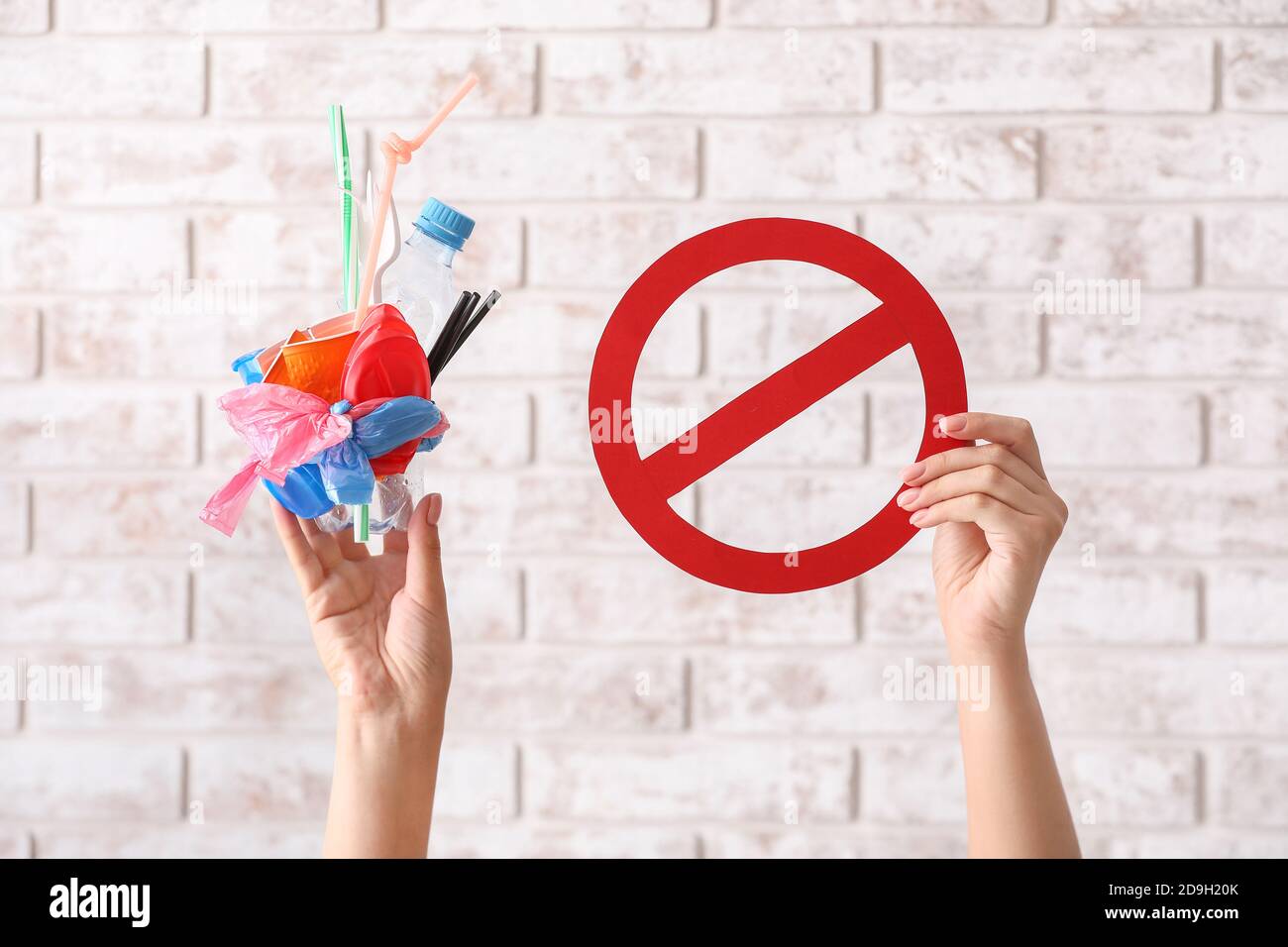 Female hands with plastic garbage and stop sign on brick background ...