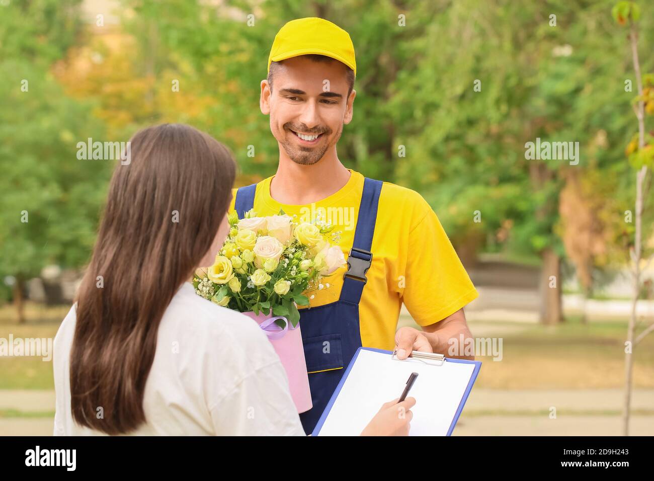 Young woman receiving beautiful flowers from delivery man outdoors ...