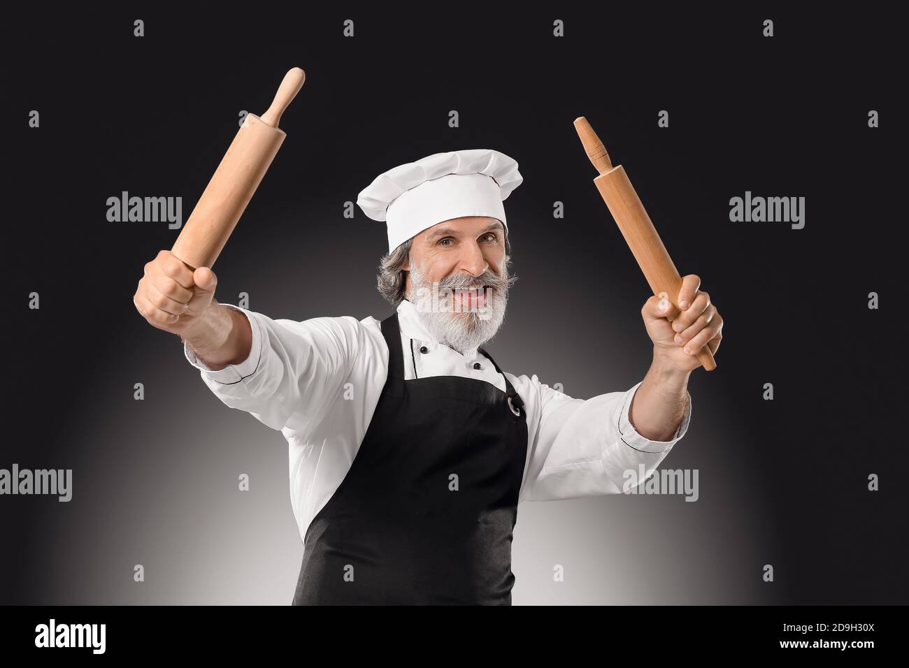 Mature male chef with rolling pins on dark background Stock Photo - Alamy