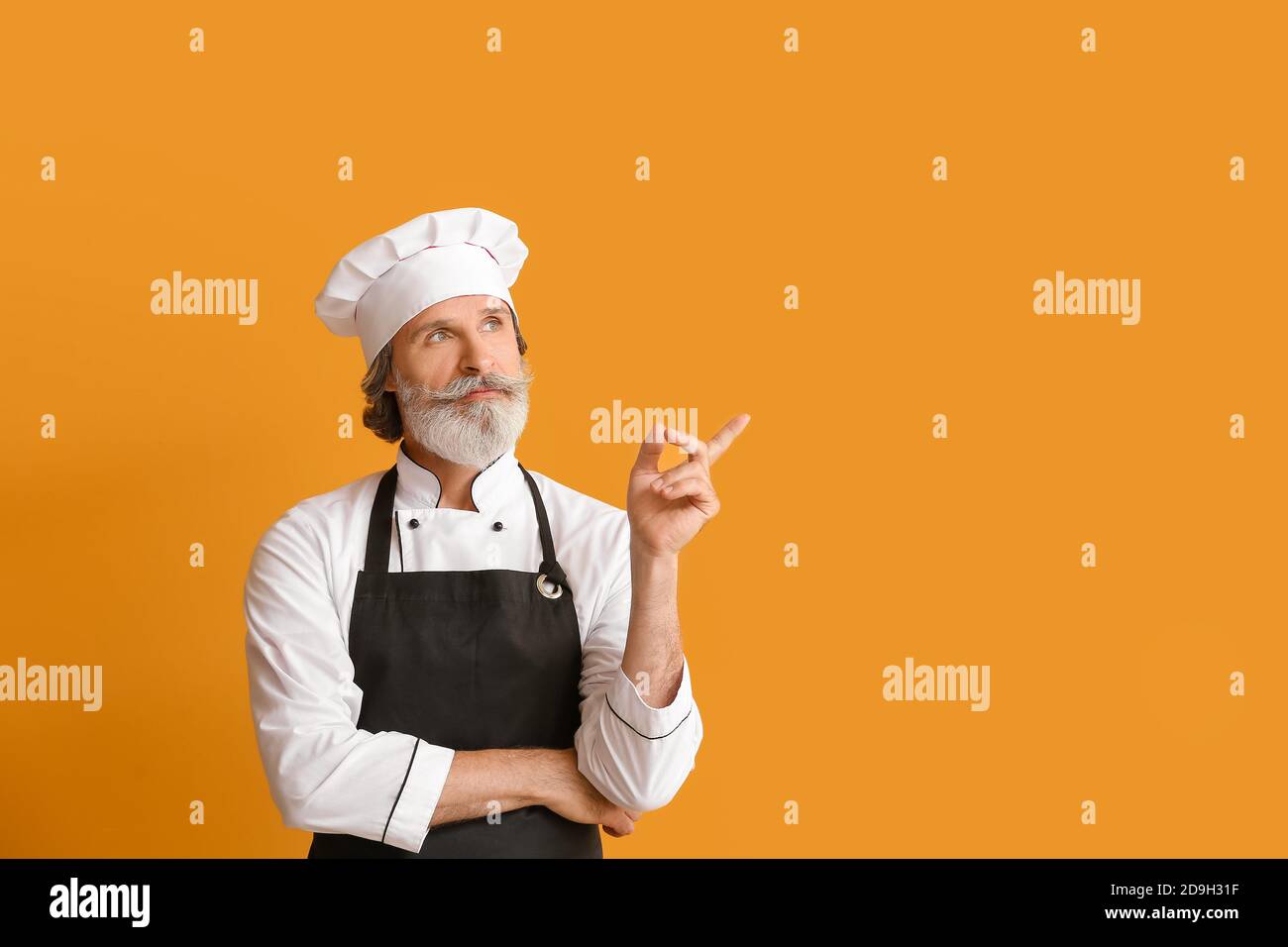 Mature male chef pointing at something on color background Stock Photo ...