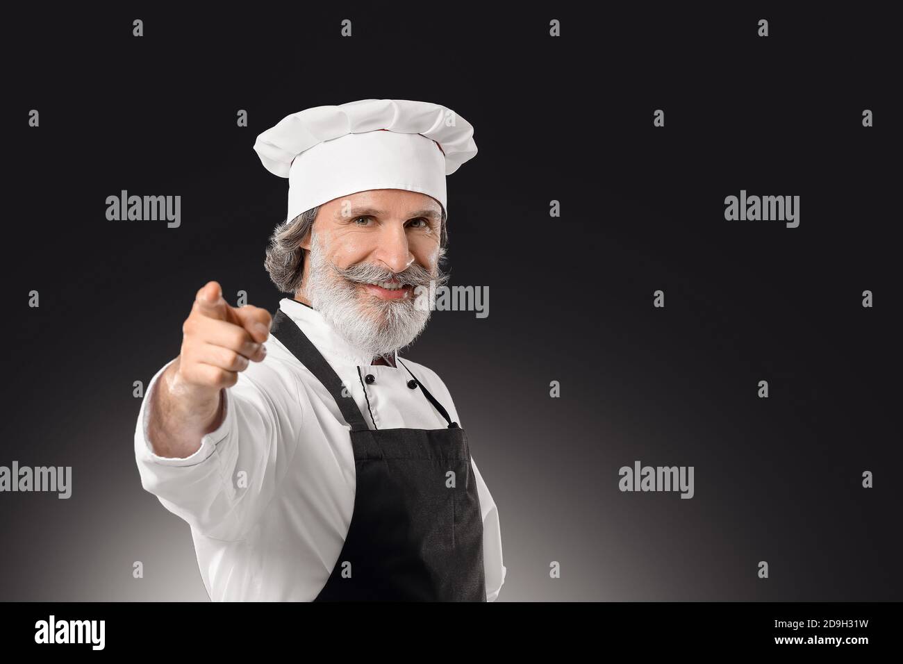 Mature male chef pointing at viewer on dark background Stock Photo - Alamy