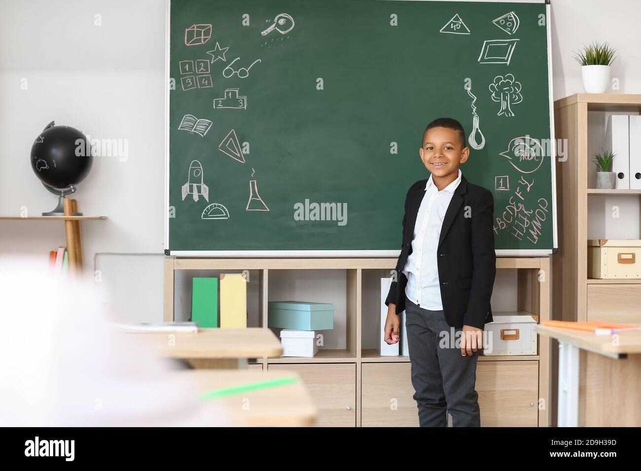 Cute little African-American schoolboy near blackboard in classroom ...