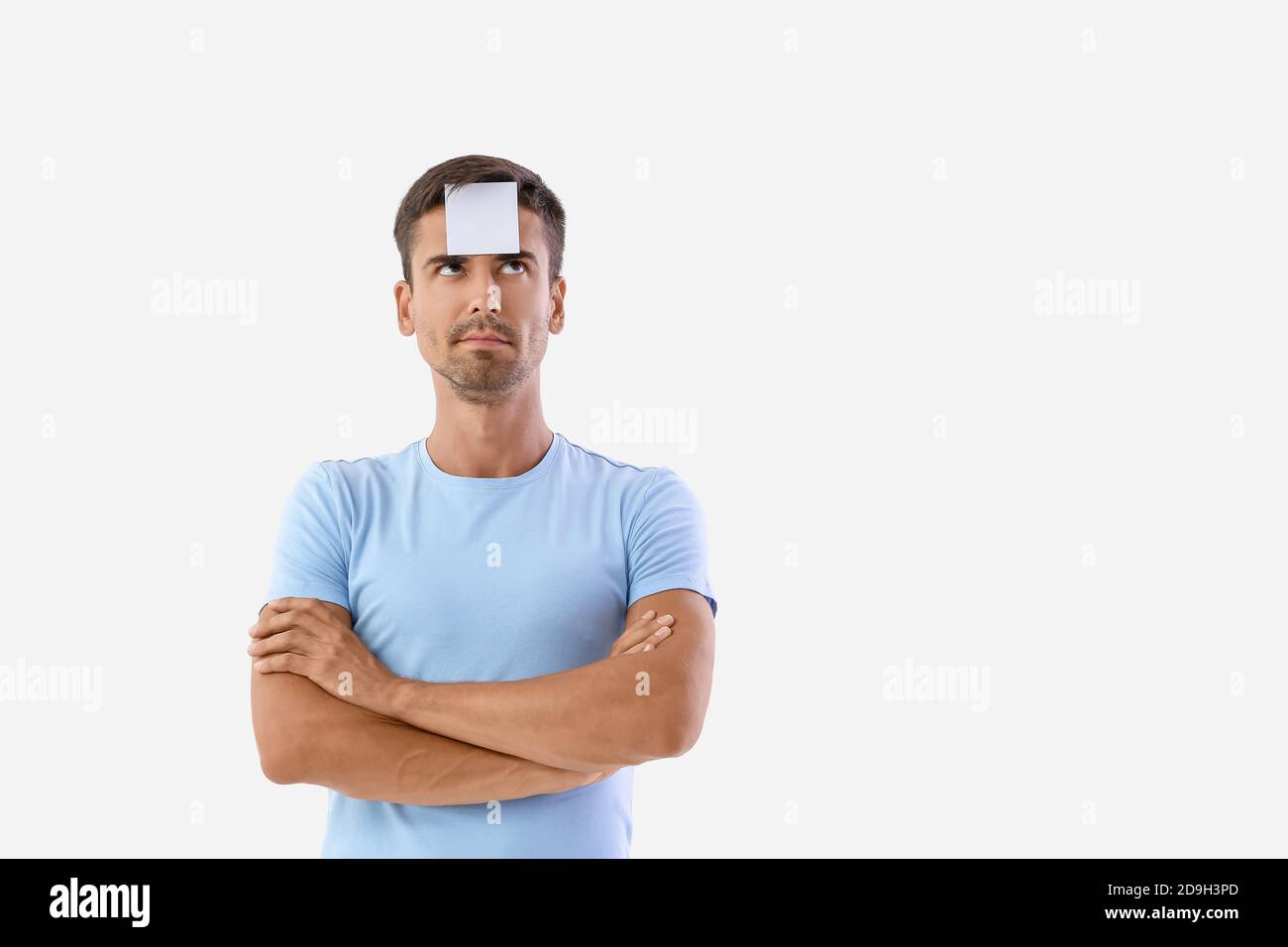 Displeased young man with small blank paper sheet on his forehead ...