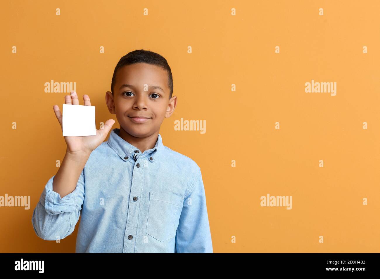 Little African-American boy with blank note paper on color background ...