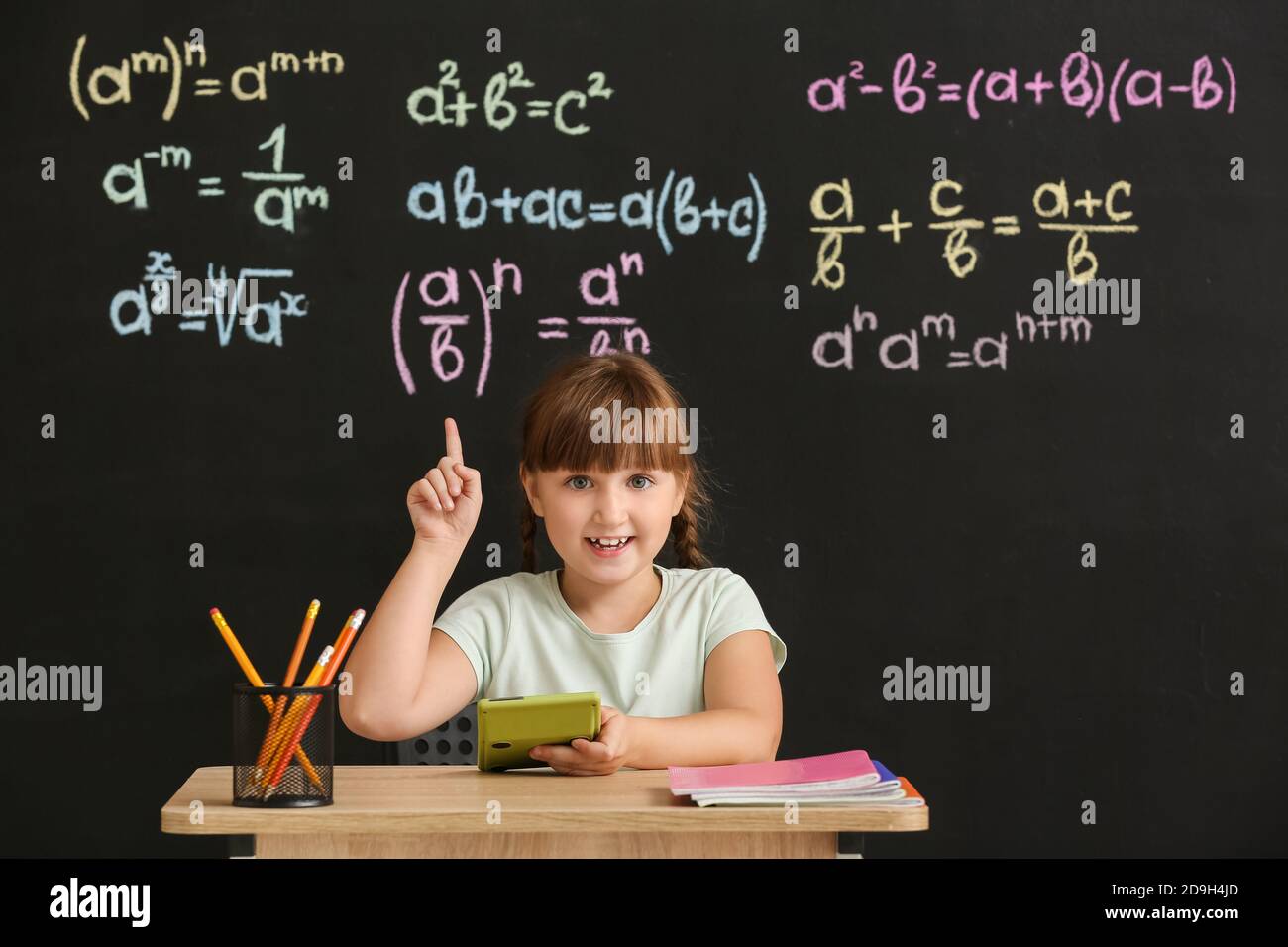Cute pupil with calculator sitting at desk during lesson in classroom ...