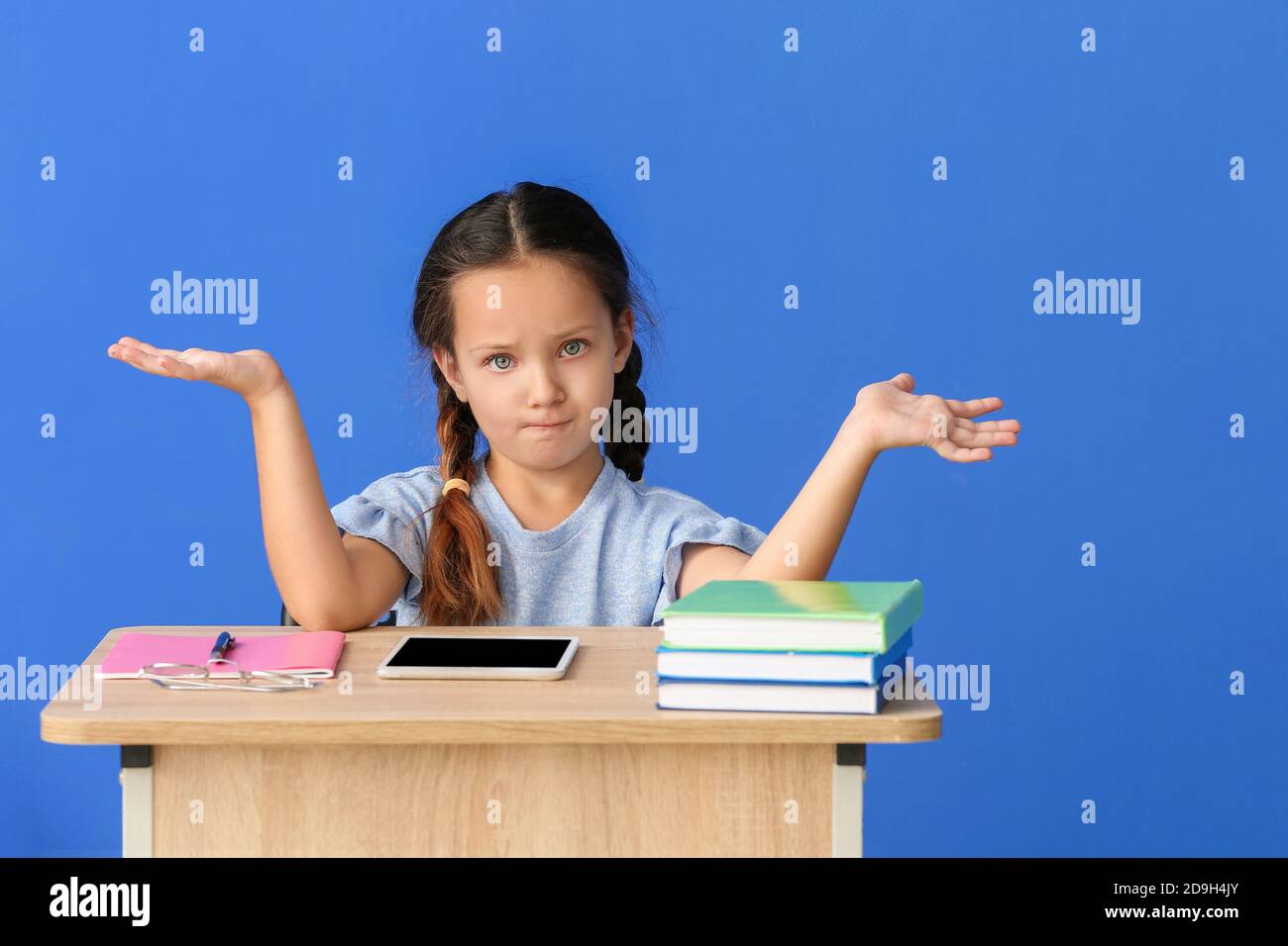 Confused pupil sitting at desk against color background Stock Photo - Alamy