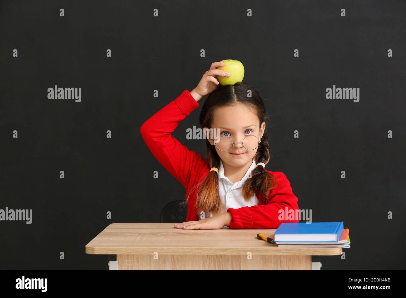 Little pupil sitting at school desk against dark background Stock Photo ...