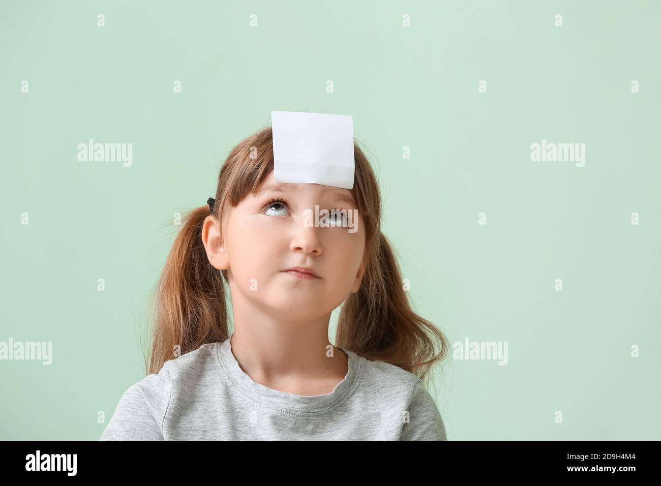 Little girl with blank note paper on her forehead against color ...