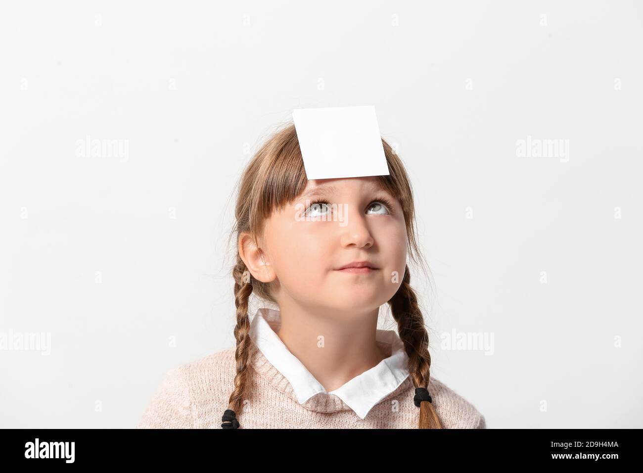 Little girl with blank note paper on her forehead against light ...