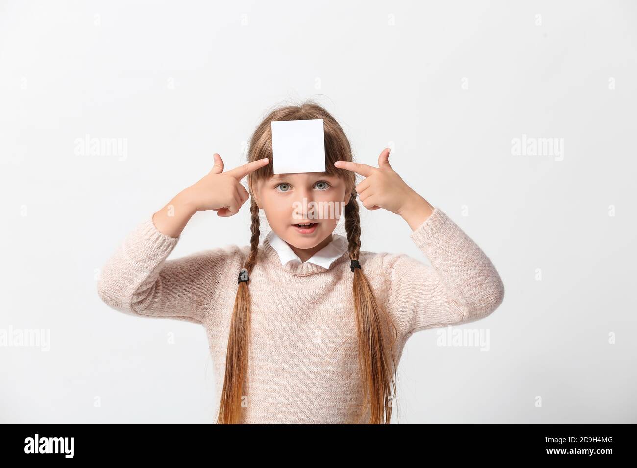 Little girl with blank note paper on her forehead against light ...