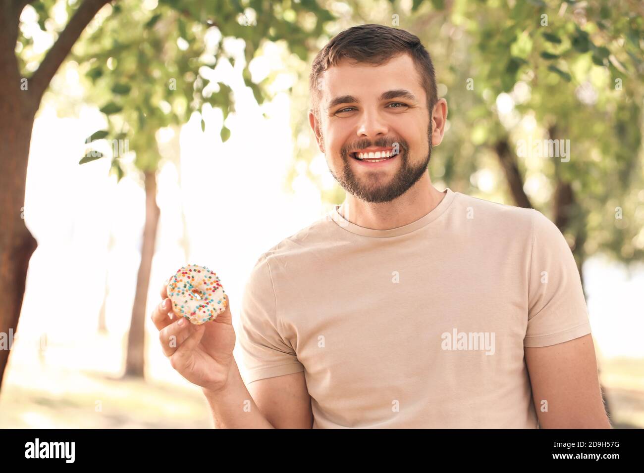 Handsome young man eating sweet donut outdoors Stock Photo - Alamy