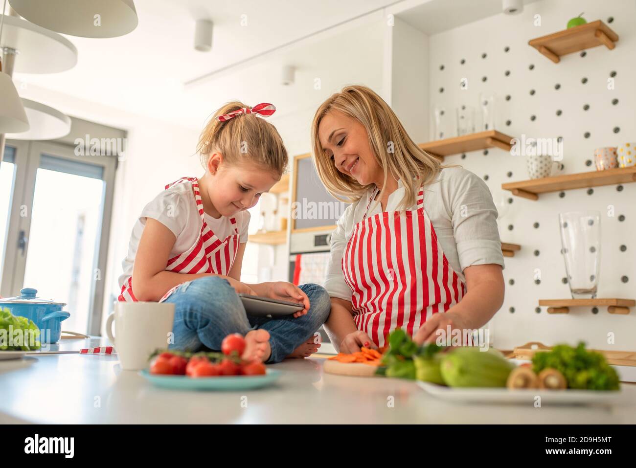 Cute daughter playing on the phone while the mother is cooking Stock ...