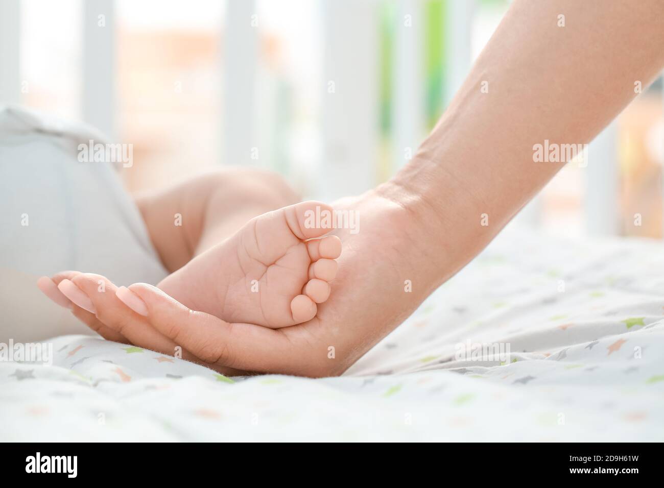 Mother's hand holding tiny leg of her baby lying in crib Stock Photo ...