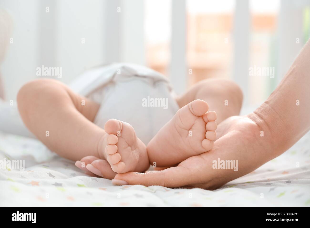 Mother's hand holding tiny legs of her baby lying in crib Stock Photo ...