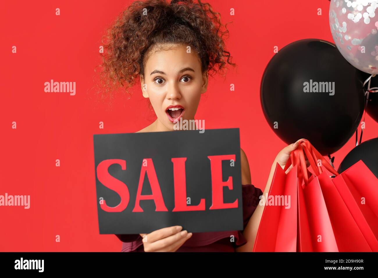 Shocked African-American woman with shopping bags and balloons on color ...