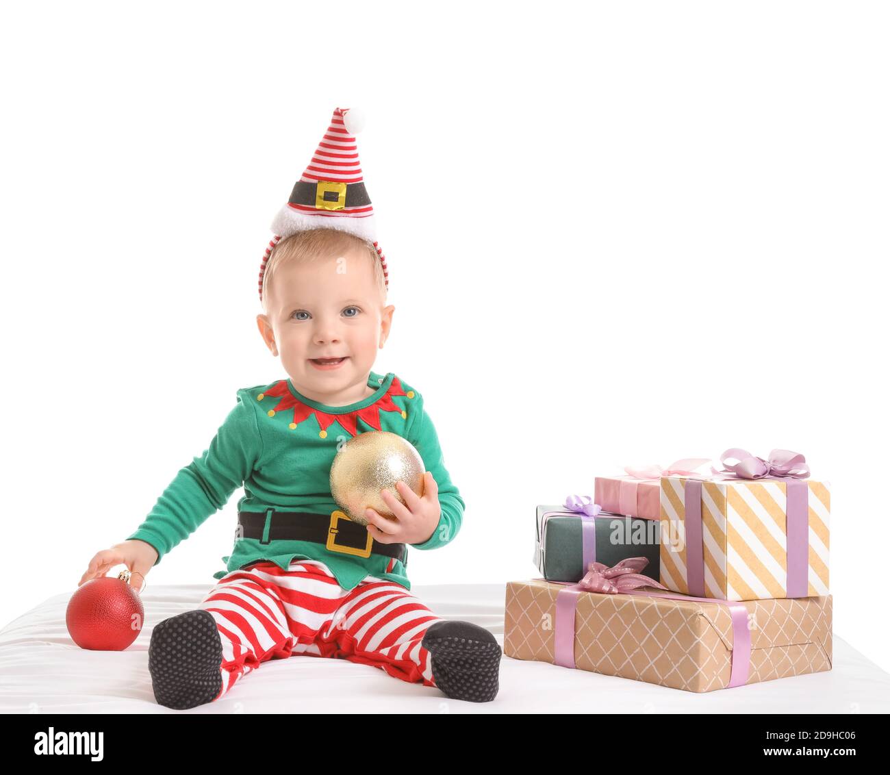 Cute little baby in Christmas elf costume and with gifts on white ...
