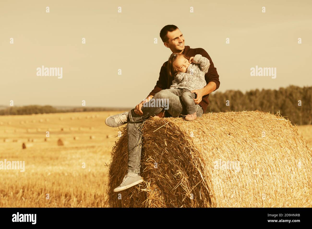 Happy father and two year old girl sitting on hay bale in harvested ...