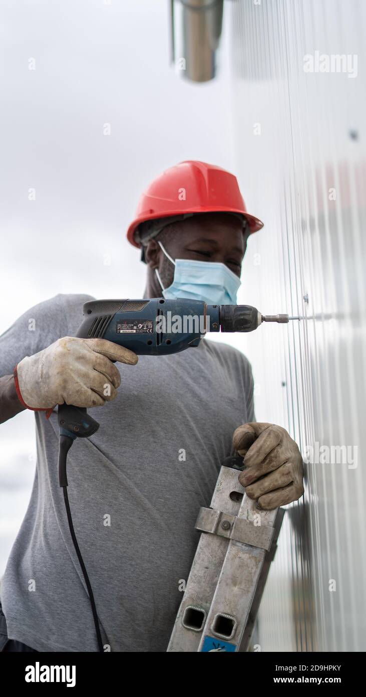 Afro-American craftsman drilling a wall with a drill machine Stock ...