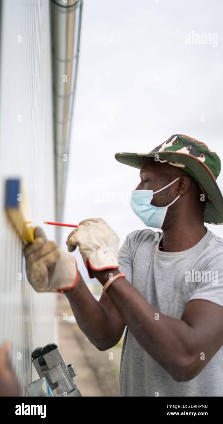Afro-American builder wearing a face mask and measuring the length of ...