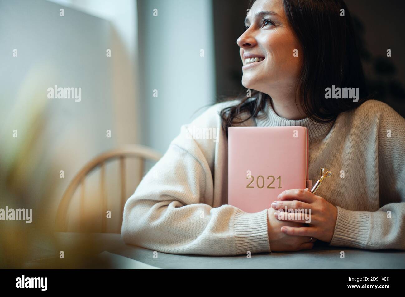 Inspired young woman with a smile looking through window and holding ...