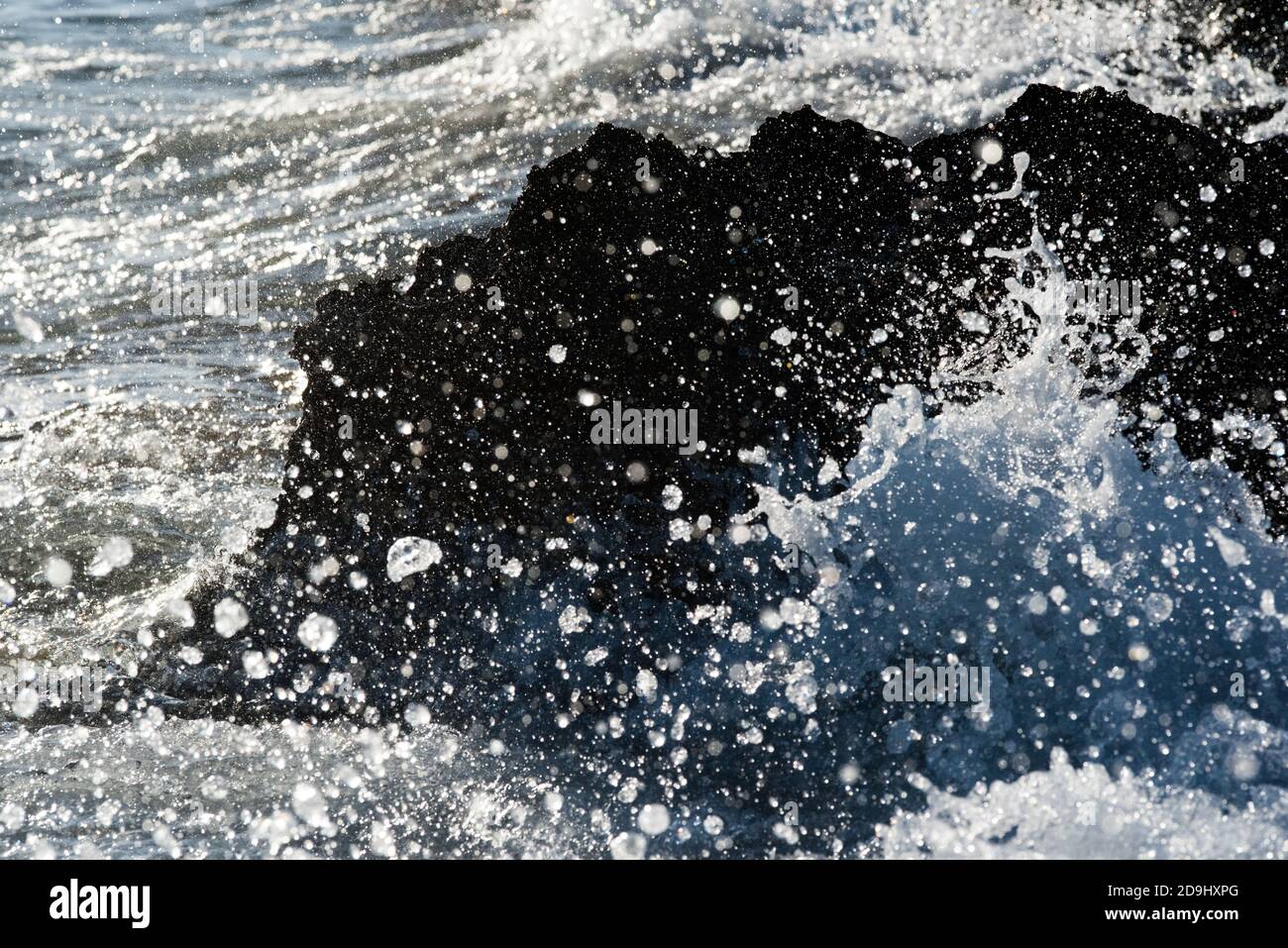 Detail of a wave breaking on the shore against a rock, splashing many ...