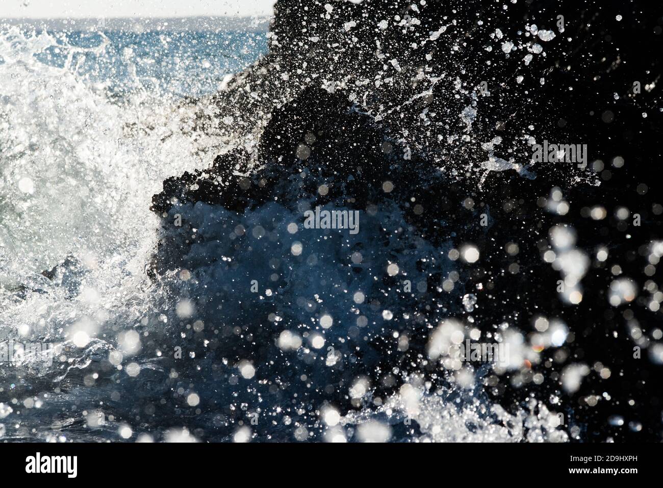 Detail of a wave breaking on the shore against a rock, splashing many ...