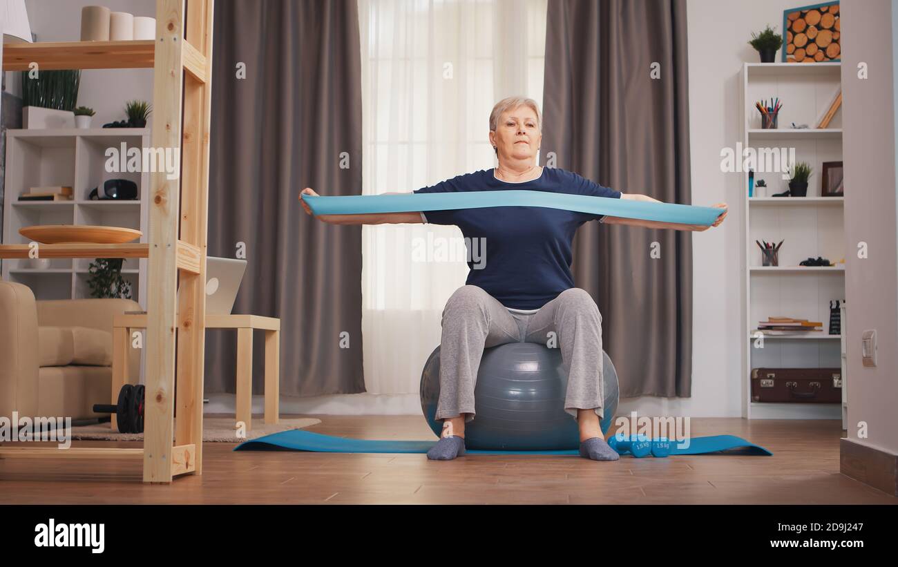 Old woman exercising with resistance band sitting on fitness ball. Old ...