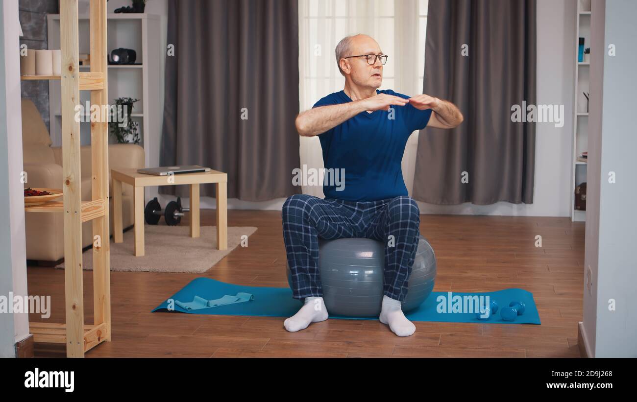 Senior man training on stability ball in living room. Old person ...