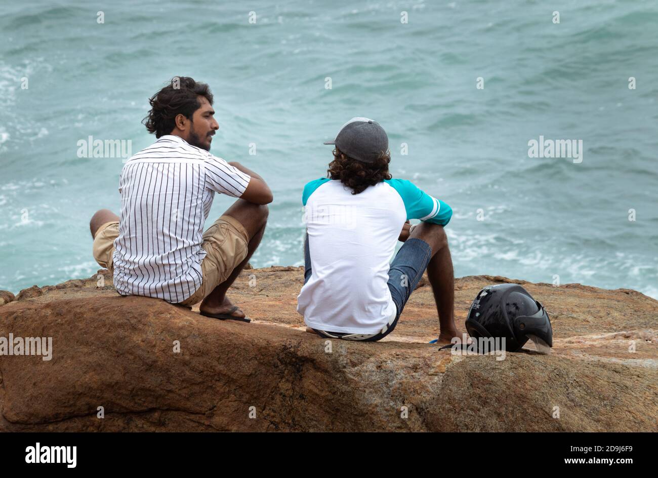 Best friends having a casual conversation on a rock on the beach ...