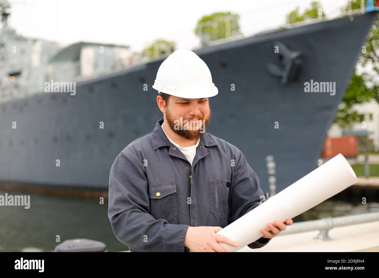 Marine assistant engineer looking at blueprints and standing near ...