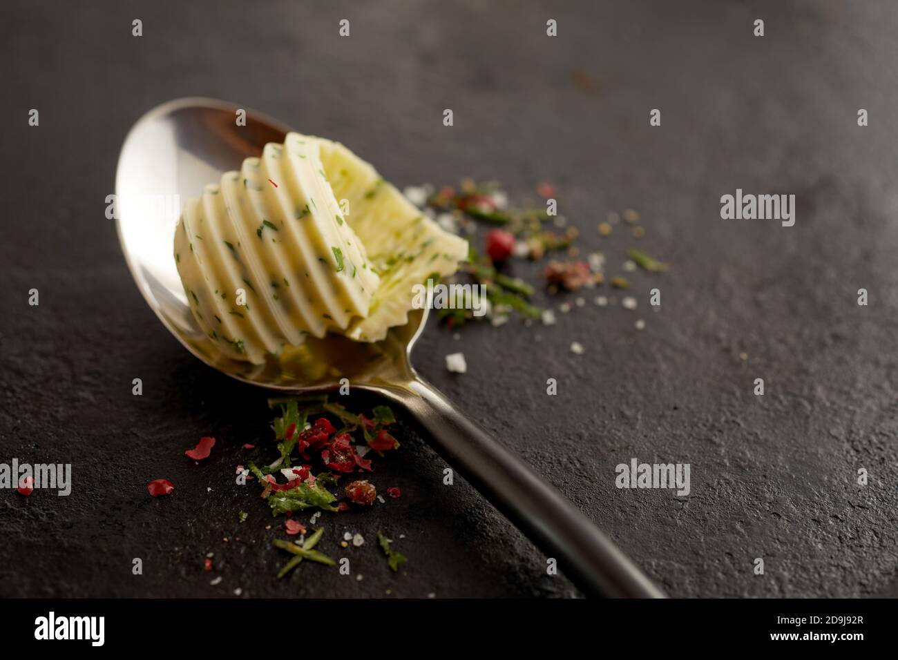 Herb flavored butter curl on a silver spoon with scattered spices and ...