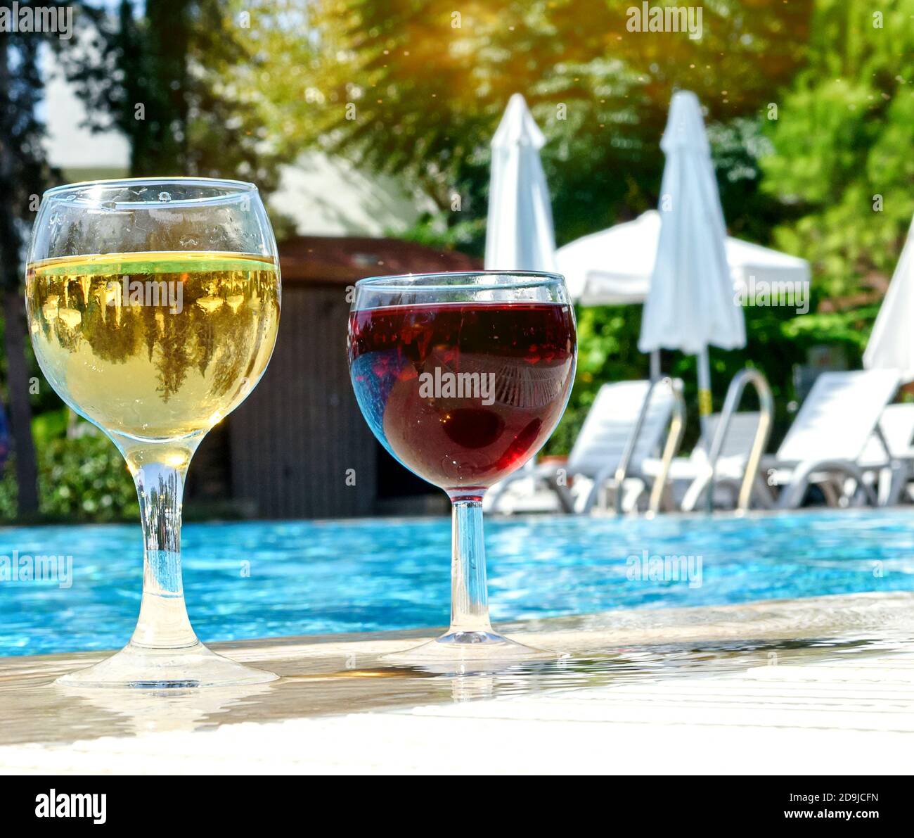 Two glasses of red and white wine are placed by the pool. The concept ...