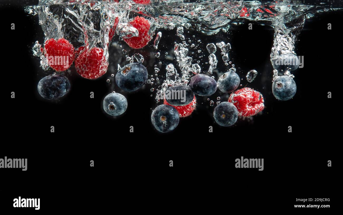 Blueberries and raspberries splashing into crystal clear water with air ...