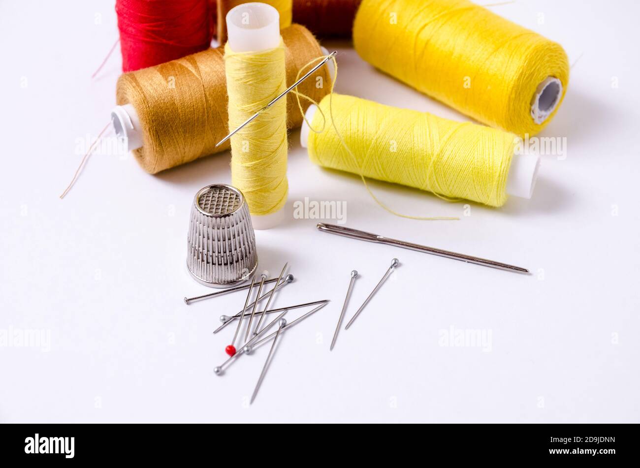Colorful spools, threads and needles and one metal thimble on white ...