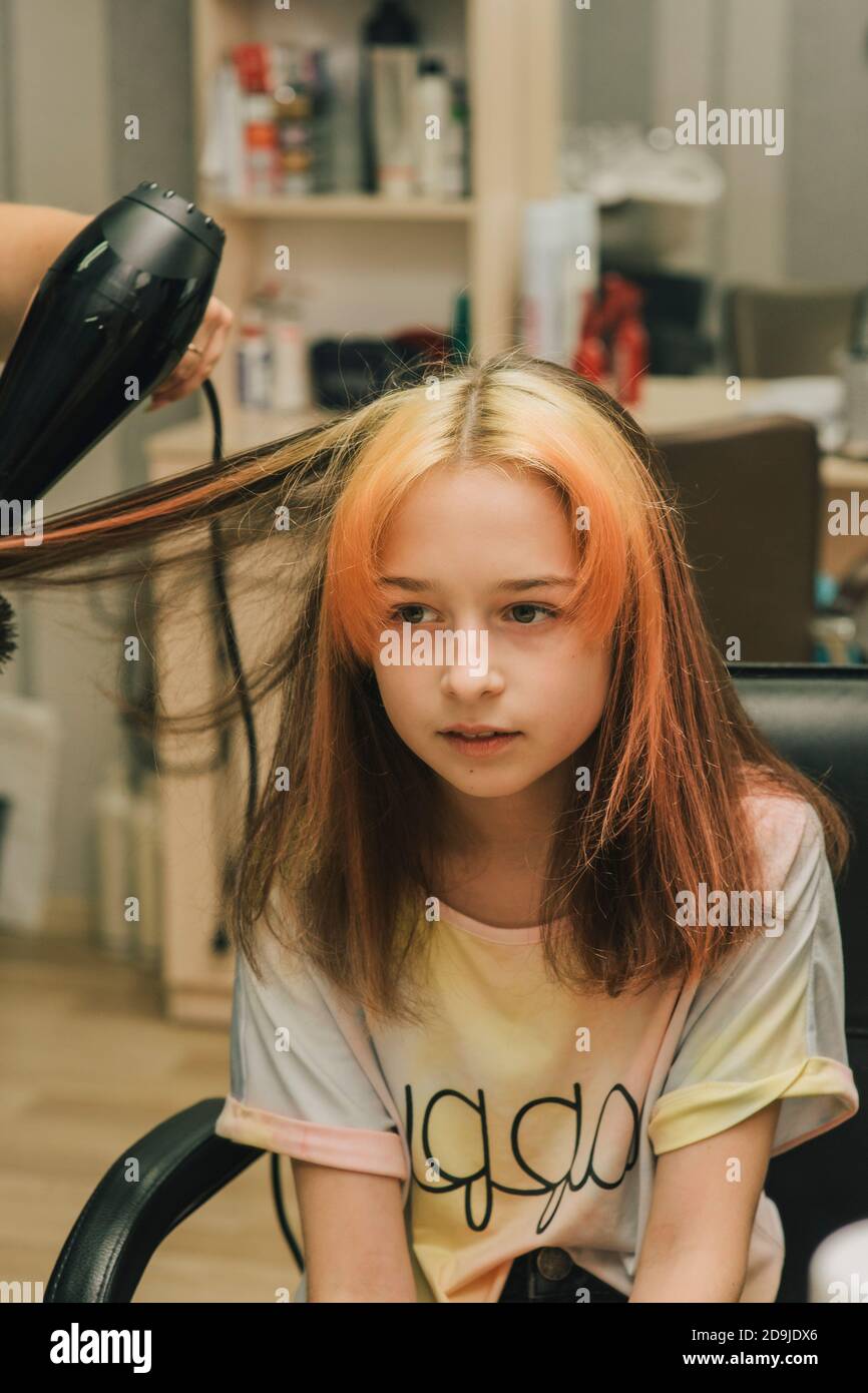 Hairdresser making a hair style to cute little girl. A teenage girl has ...