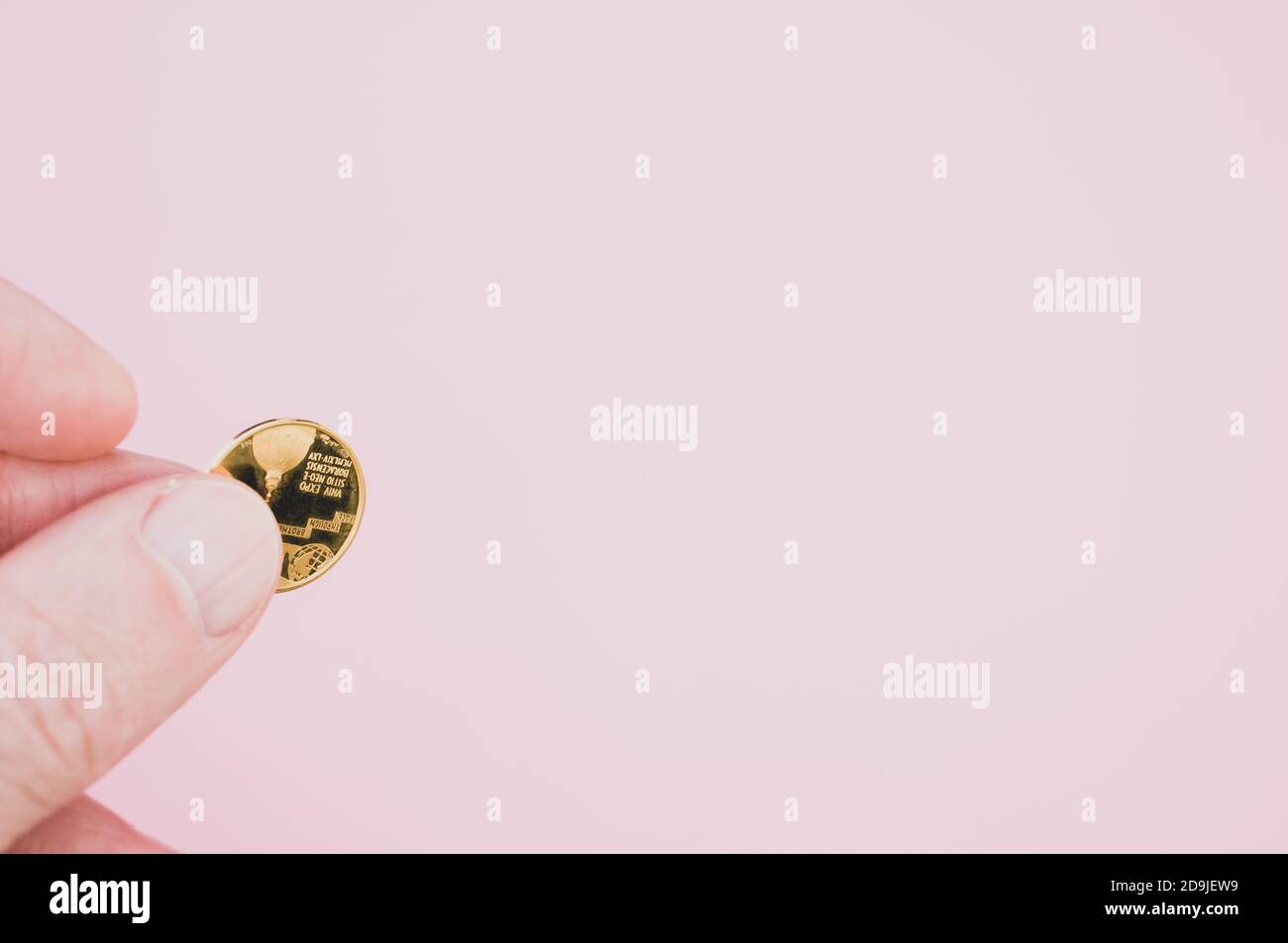 Closeup shot of a hand holding gold coin isolated on light pink ...