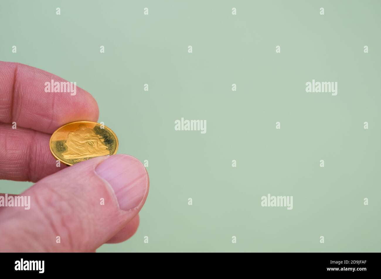 Closeup shot of a hand holding gold coin isolated on pastel green ...