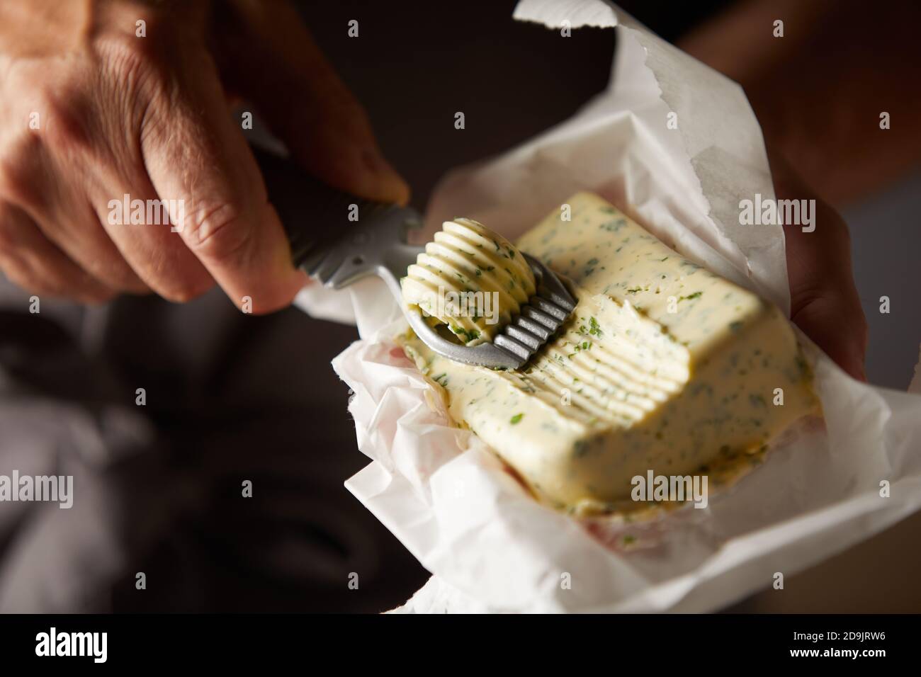 Hand of a chef cutting a butter curl off a pat of herbal butter with a ...